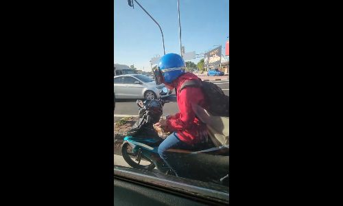 A woman eats on a motorcycle during a red light stop - zamriabdmalik